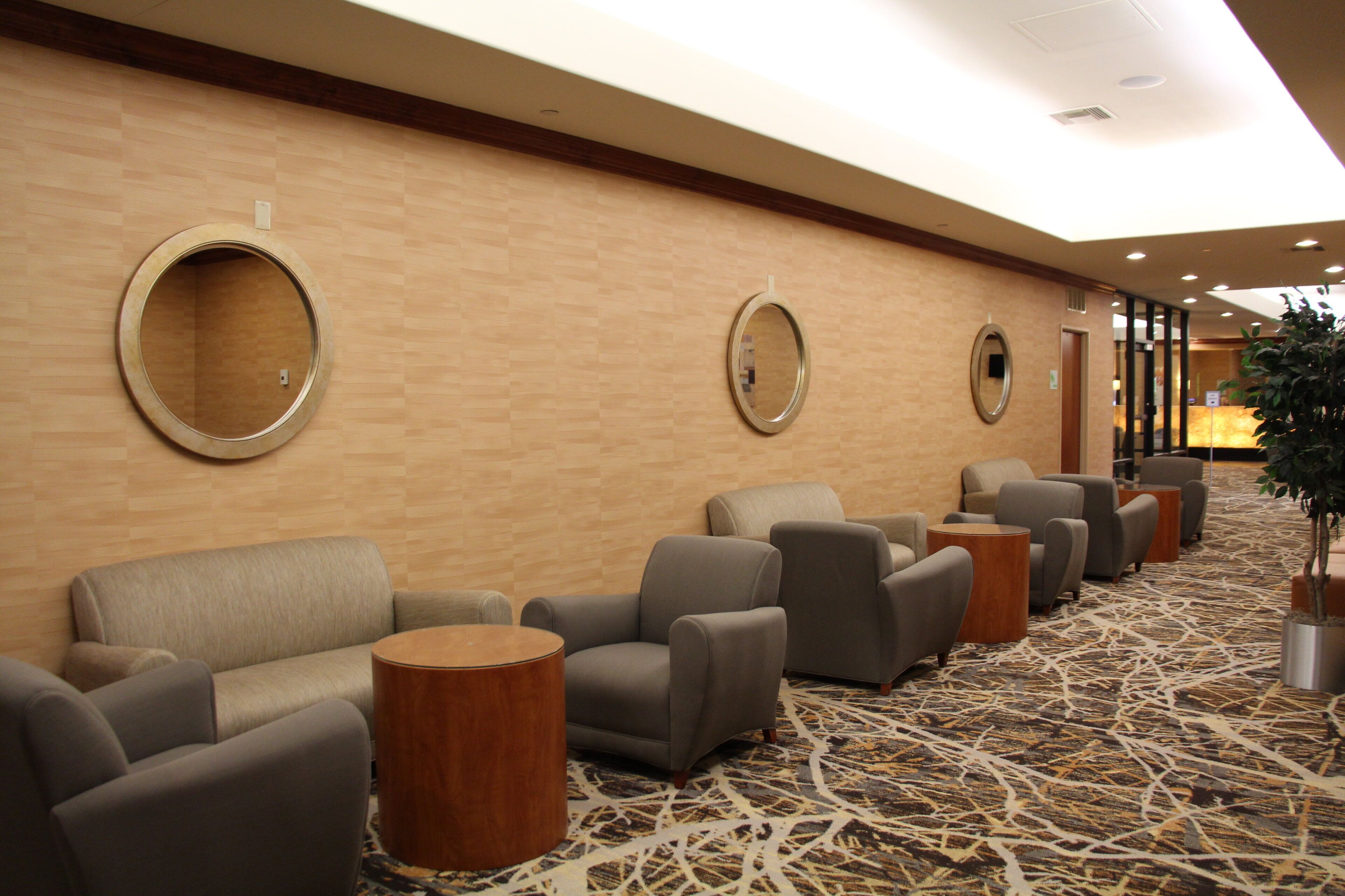Um hall de hotel com uma fileira de poltronas, um tapete estampado e espelhos fixados na parede.