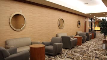 Um hall de hotel com uma fileira de poltronas, um tapete estampado e espelhos fixados na parede.