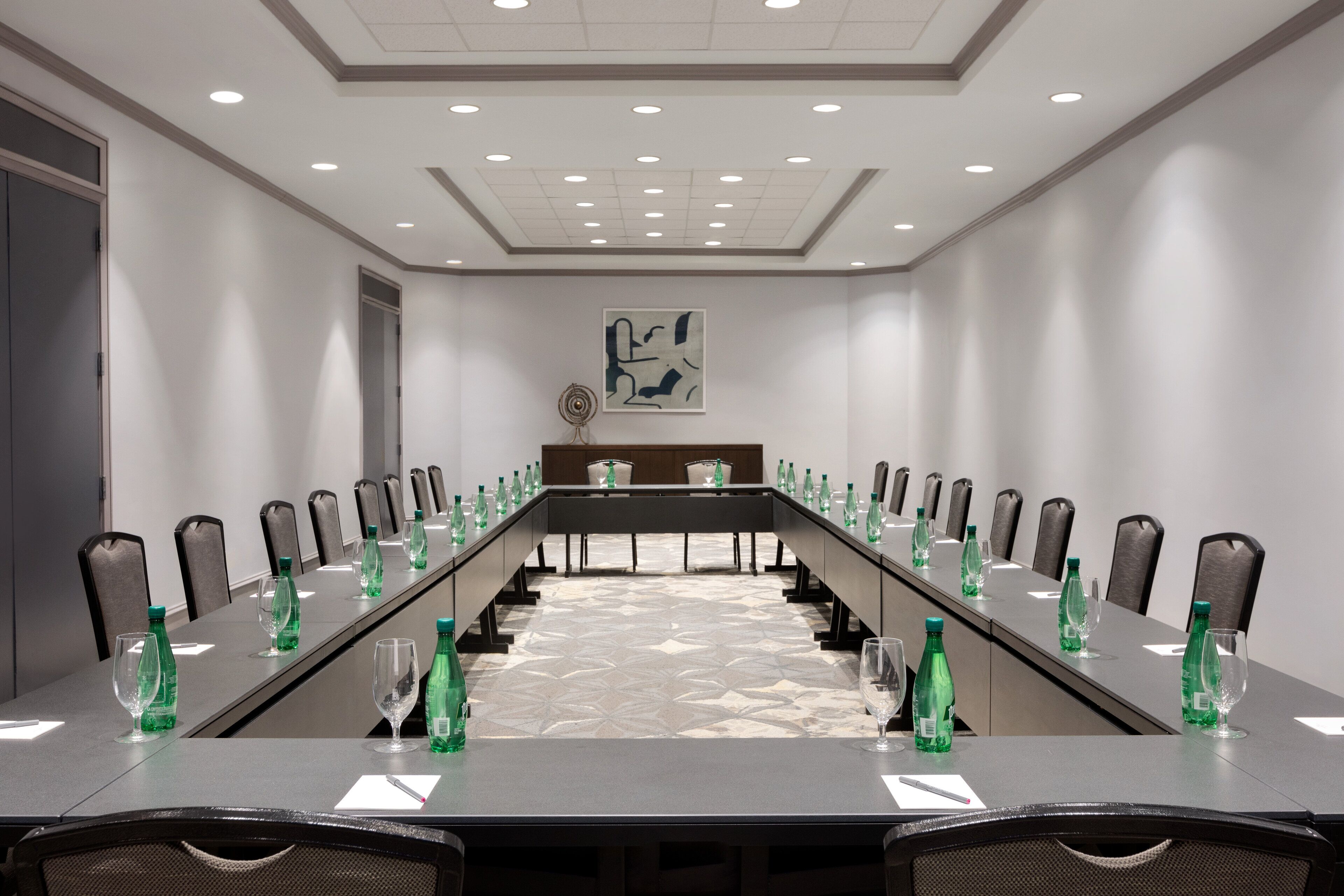 Uma sala de conferências com uma mesa comprida, cadeiras e garrafas de água.