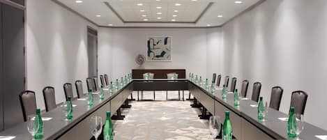 Uma sala de conferências com uma mesa comprida, cadeiras e garrafas de água.