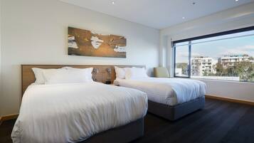 Quarto de hotel com duas camas, uma janela grande com vista para a cidade e uma pintura abstrata moderna na parede.