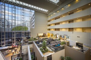 Um amplo átrio com vários níveis, grandes janelas e uma área de estar central com sofás e mesas.