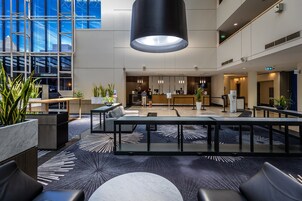 Um lobby moderno com balcão de recepção, área de estar e amplas janelas com vista para a paisagem urbana.