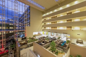 Um átrio de hotel com vários níveis, fachada de vidro, diversos andares e diferentes áreas de estar.