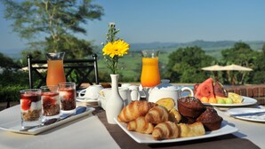 Uma mesa de café da manhã com croissants, frutas e bebidas, com uma vista panorâmica.