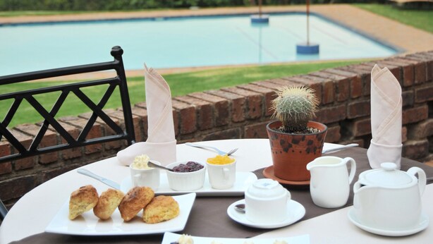 Uma mesa posta para um chá, com vista para uma piscina e colinas ao fundo.