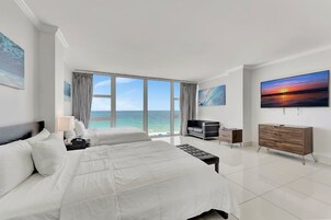 Quarto de hotel com uma cama grande, televisão, penteadeira e vista para o oceano.
