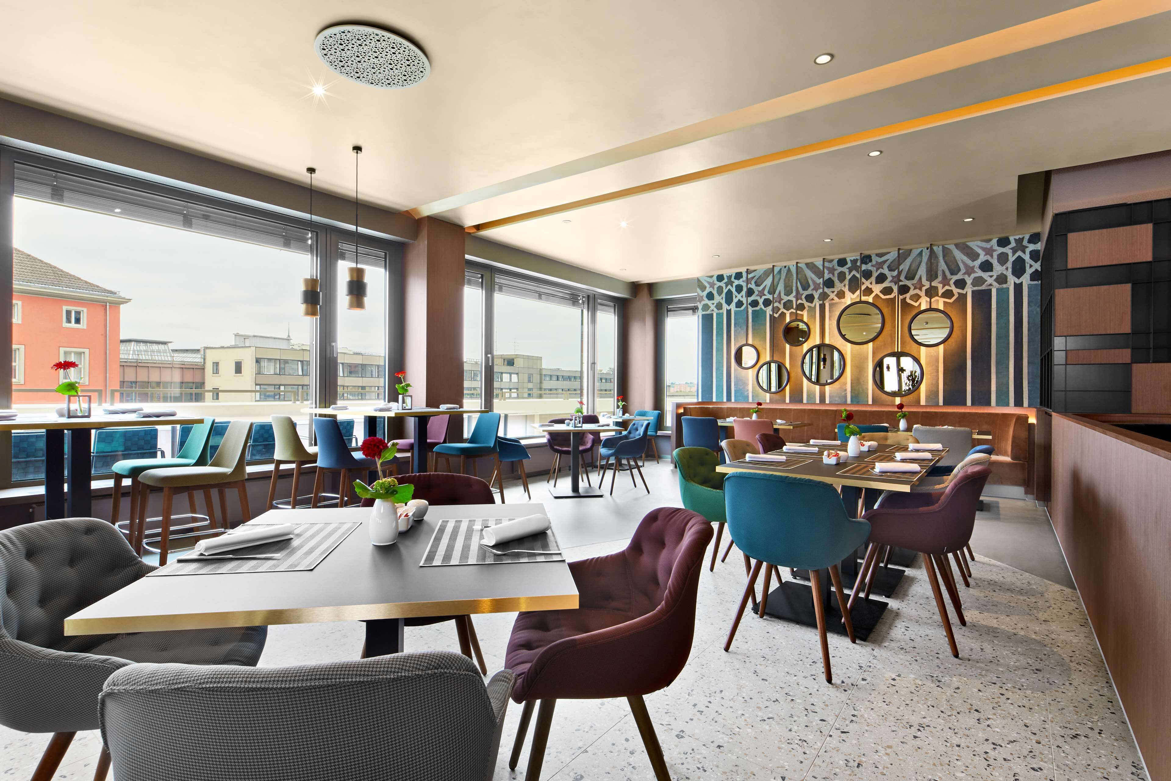 Um restaurante moderno com grandes janelas, diferentes opções de assento e uma parede decorativa com espelhos circulares.