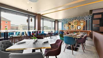 Um restaurante moderno com grandes janelas, diferentes opções de assento e uma parede decorativa com espelhos circulares.