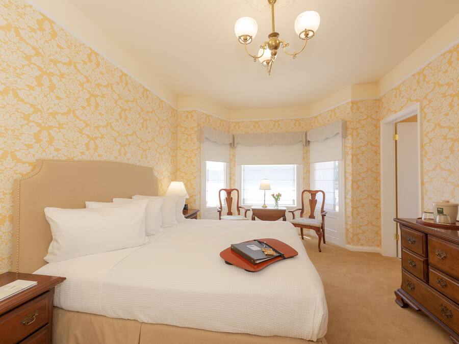 Quarto de hotel com uma cama grande, penteadeira, televisão e janela com cortinas.