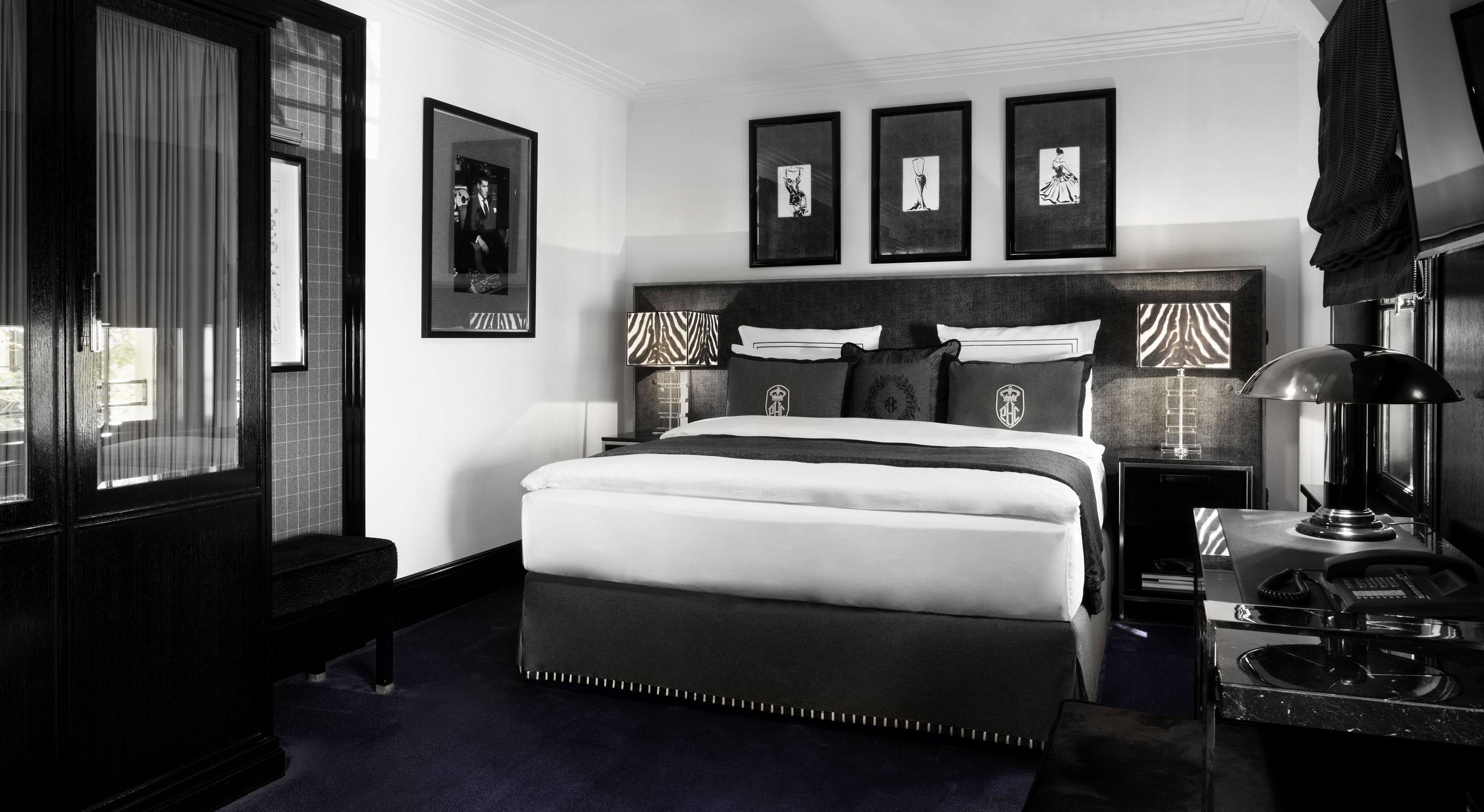 Quarto de hotel moderno com uma cama grande, luminárias nas mesinhas de cabeceira, uma escrivaninha com abajur e quadros na parede.