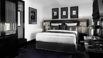 Quarto de hotel moderno com uma cama grande, luminárias nas mesinhas de cabeceira, uma escrivaninha com abajur e quadros na parede.