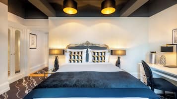 Quarto de hotel com uma cama grande, duas luminárias de cabeceira, uma escrivaninha com cadeira e um guarda-roupa.