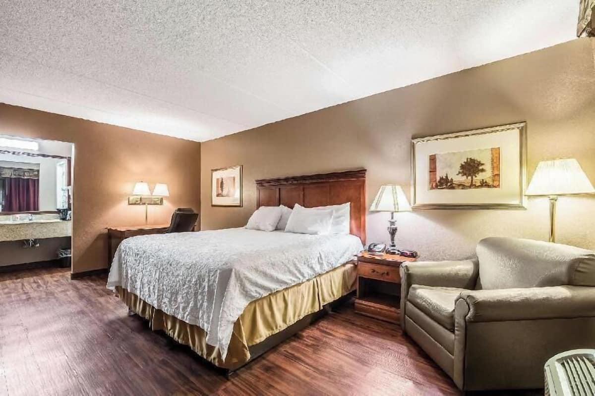 Quarto de hotel com cama, mesas de cabeceira, uma cadeira e um quadro na parede.