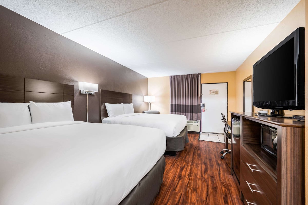 Quarto de hotel com duas camas, televisão, escrivaninha e guarda-roupa.