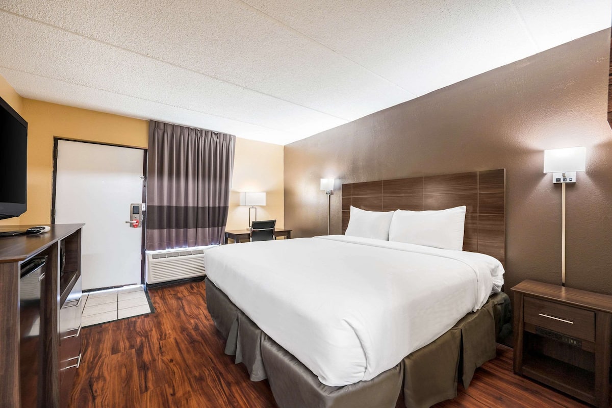 Quarto de hotel com uma cama grande, uma escrivaninha com cadeira, televisão e abajur.