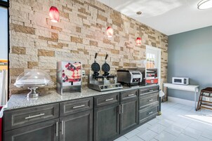 Cozinha com parede de pedra, máquina de waffles, cafeteira e micro-ondas.
