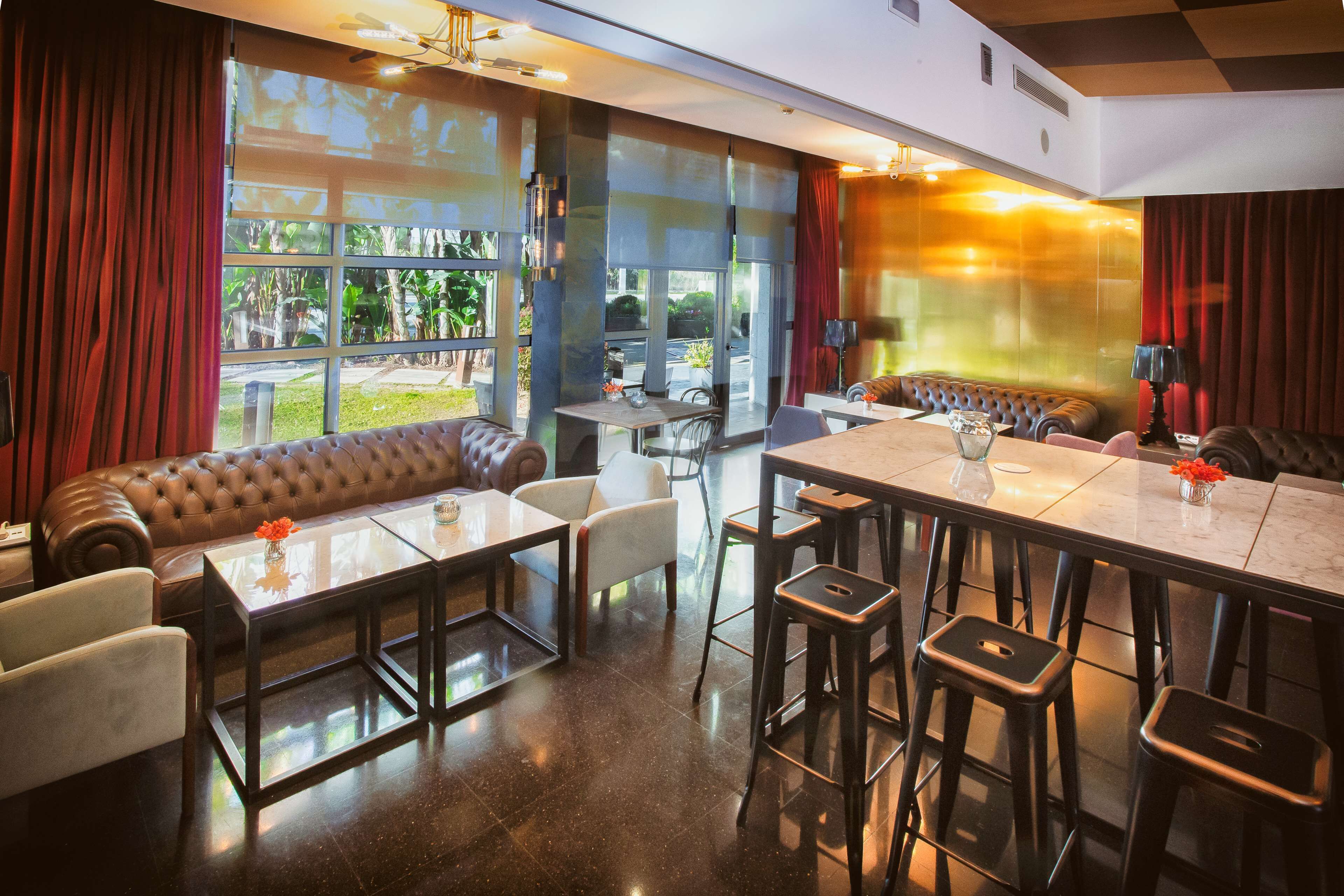 Uma área de bar moderna com disposição de banquetas, um banco acolchoado e uma mesa de vidro.