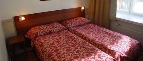 Cama de casal com roupa de cama floral, mesa de cabeceira, quadro emoldurado na parede e janela com cortinas.
