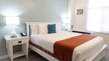 Cama bem arrumada com roupa de cama branca e um cobertor marrom, mesa de cabeceira com abajur e uma pequena gaveta.