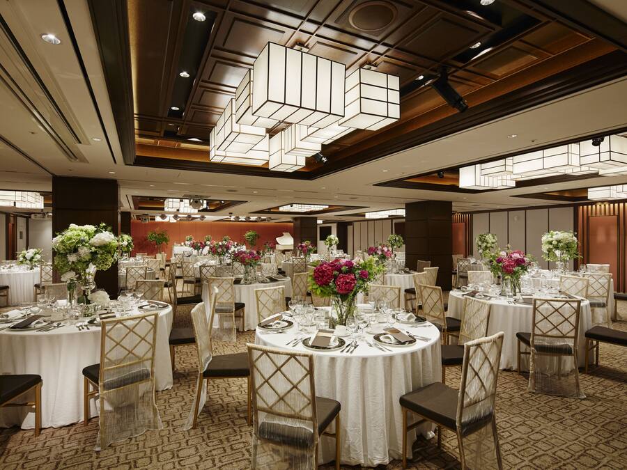 Uma sala de banquetes com mesas redondas dispostas para refeições, com toalhas brancas, cadeiras e centros de mesa florais.