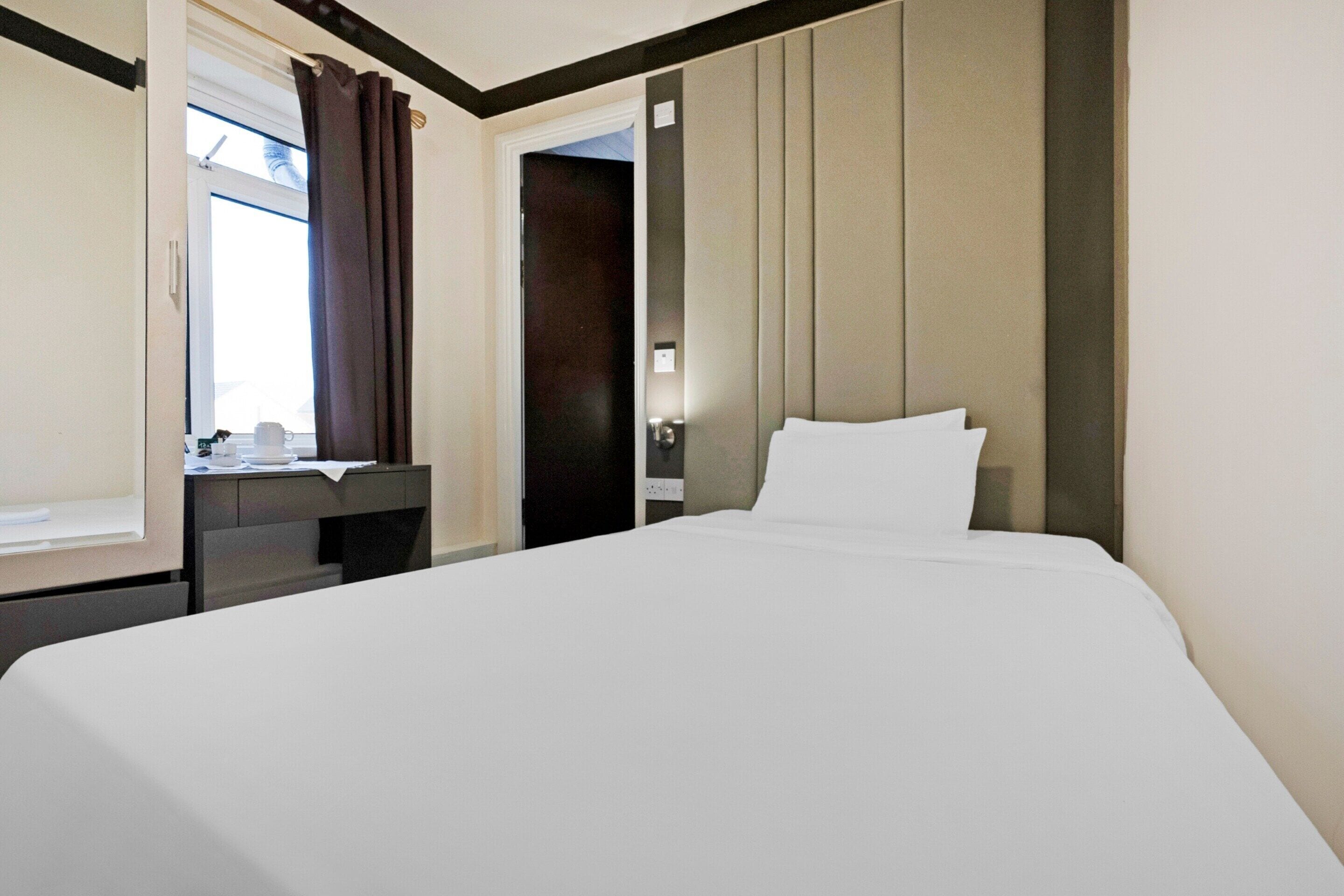 Quarto de hotel com uma cama grande, uma escrivaninha com cadeira, um espelho e uma porta que dá para outro aposento.