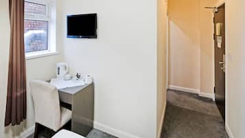 Quarto de hotel pequeno com escrivaninha, cadeira, televisão e janela com cortinas.
