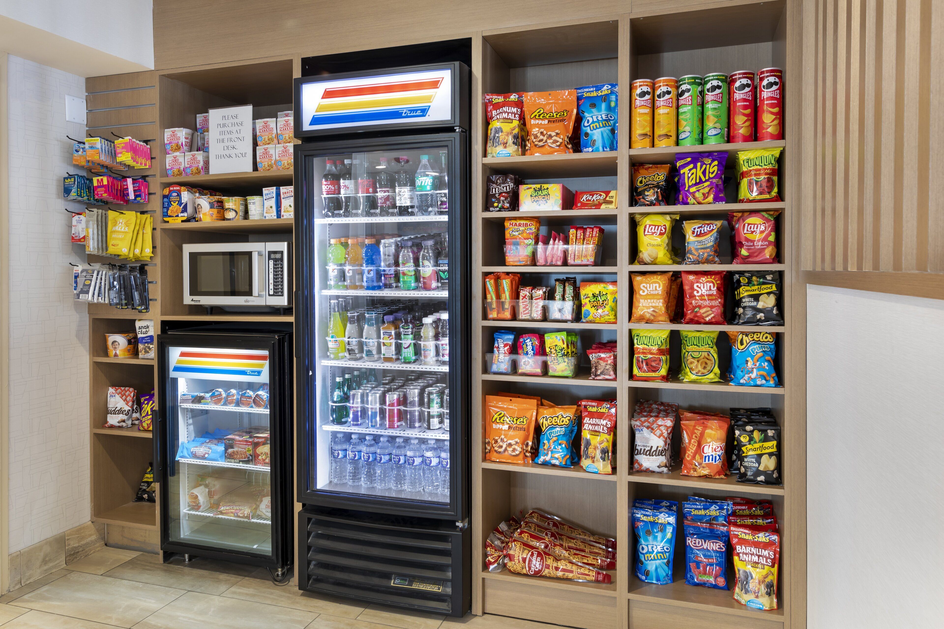 Uma máquina de venda automática com lanches e bebidas, um micro-ondas e prateleiras com diversos produtos embalados.