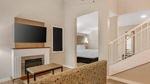 Uma sala de estar moderna com lareira, um sofá, uma TV e uma escada que leva a um quarto.