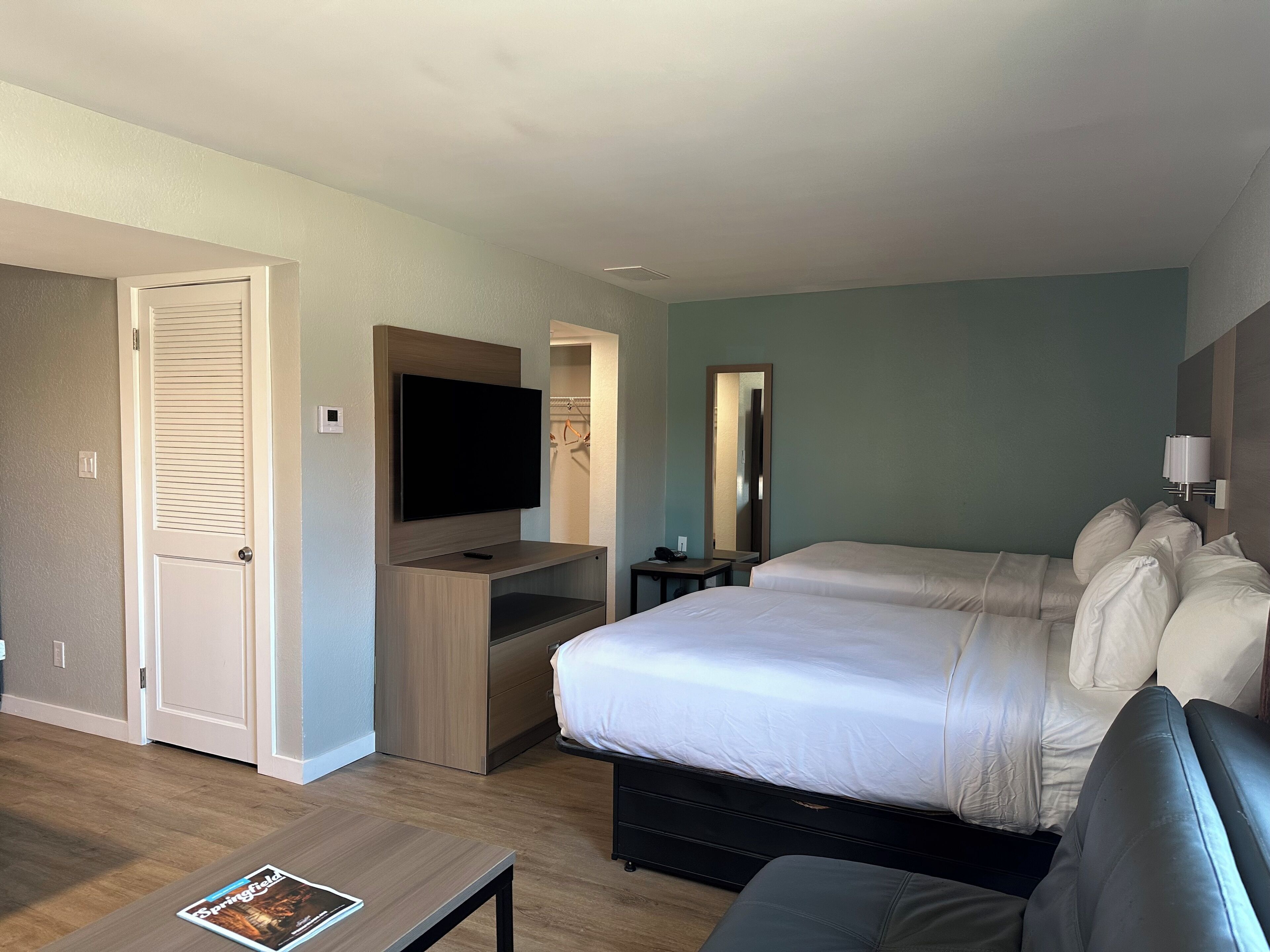 Quarto de hotel com cama, televisão, escrivaninha, espelho e armário.