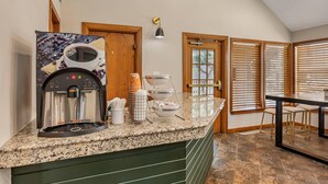 Uma área de cozinha com máquina de café, serviço de buffet e mesa de jantar com cadeiras.