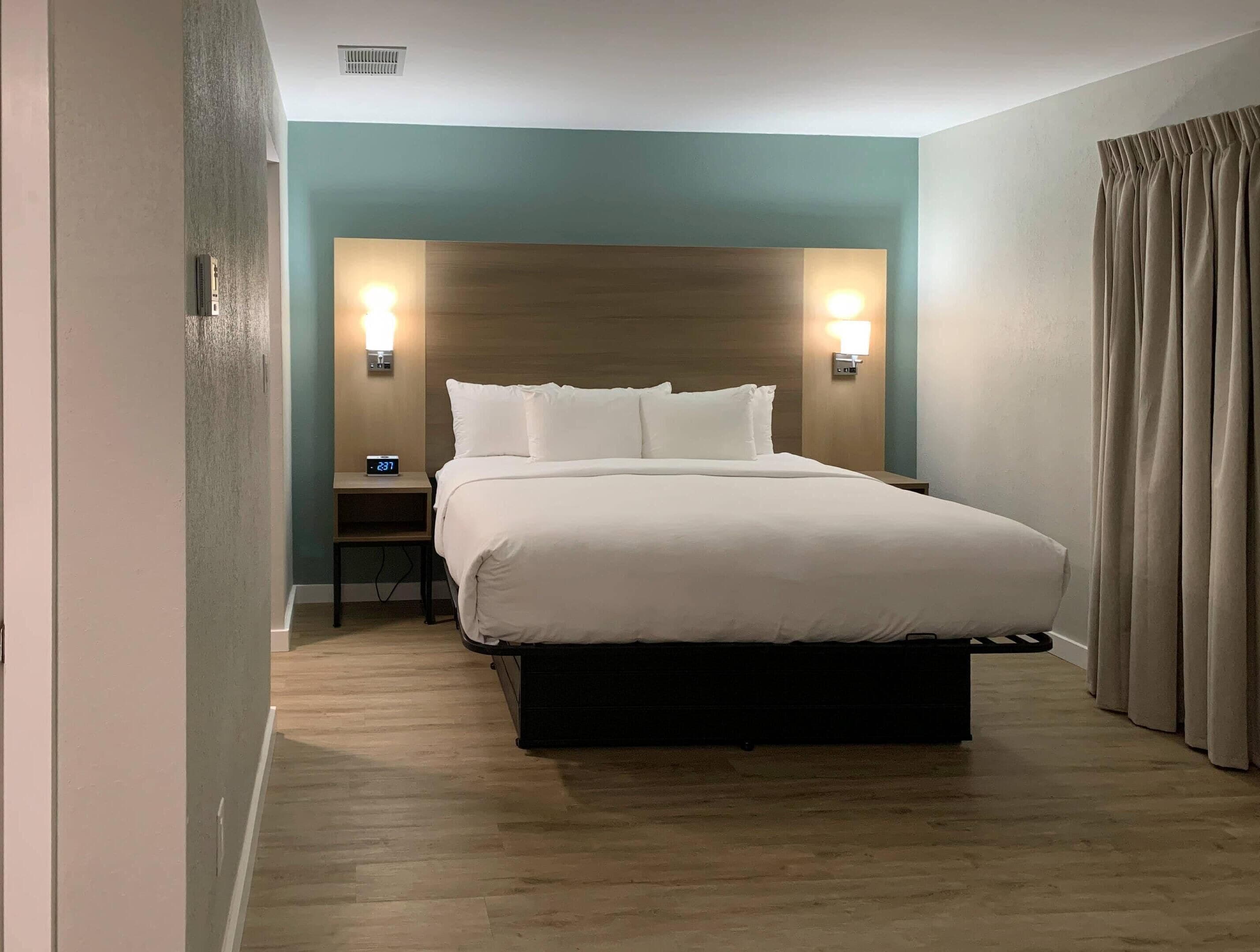 Quarto de hotel com cama grande, duas luminárias de cabeceira, mesa de apoio e aquecedor fixado na parede.