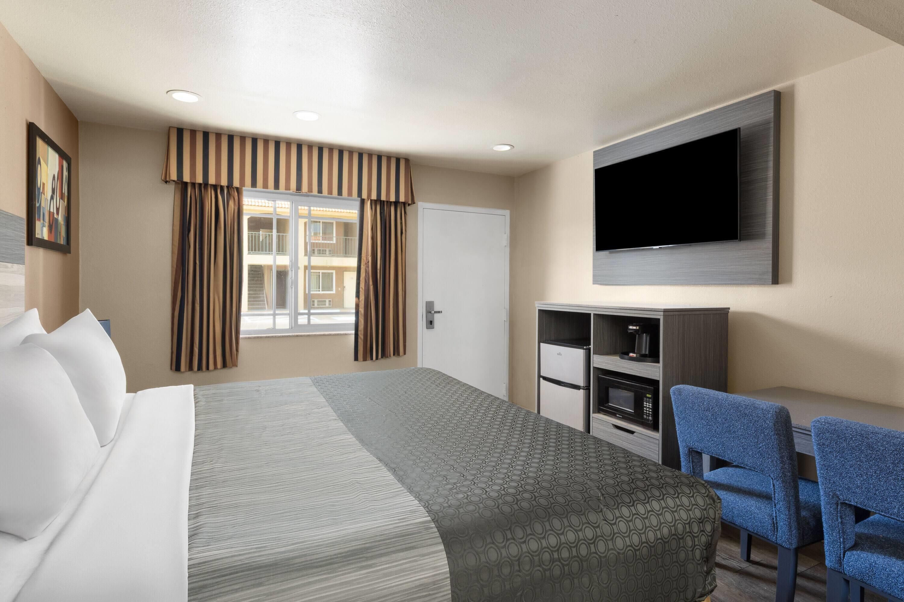 Quarto de hotel com cama, escrivaninha, televisão de tela plana, minibar e janela com cortinas.