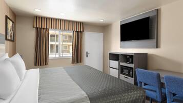 Quarto de hotel com cama, escrivaninha, televisão de tela plana, minibar e janela com cortinas.