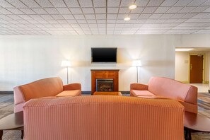 Quarto de hotel com um amplo sofá listrado, uma televisão de tela plana acima de uma lareira e duas luminárias de chão.