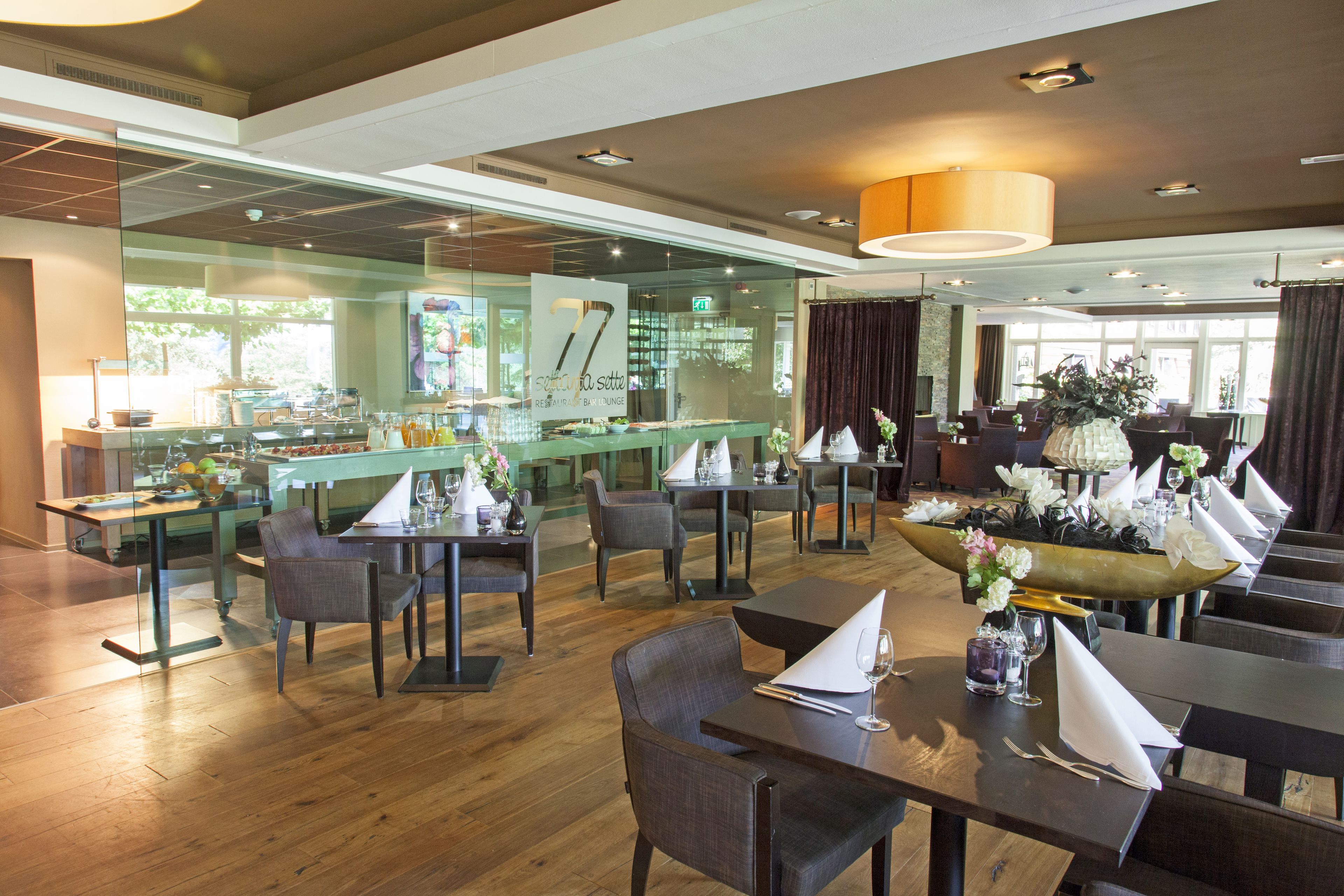 Um restaurante com soalho de madeira, mobiliário moderno e uma divisória de vidro a separar a área de refeições da cozinha.