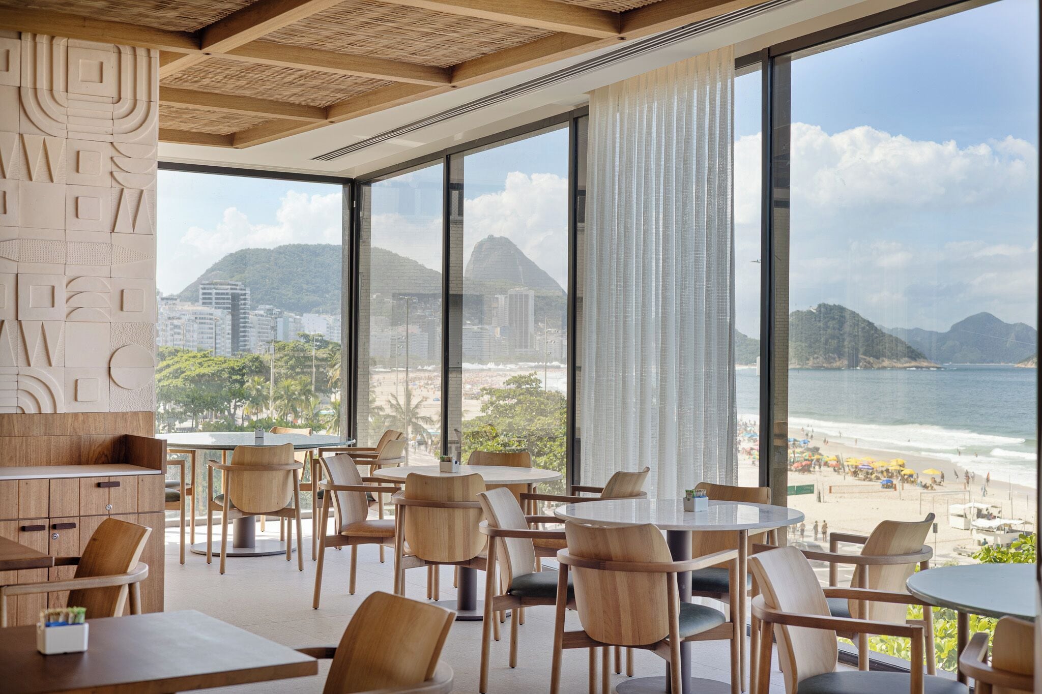 Uma área de refeições moderna com grandes janelas com vista para a praia e para a paisagem urbana.
