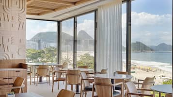 Uma área de refeições moderna com grandes janelas com vista para a praia e para a paisagem urbana.