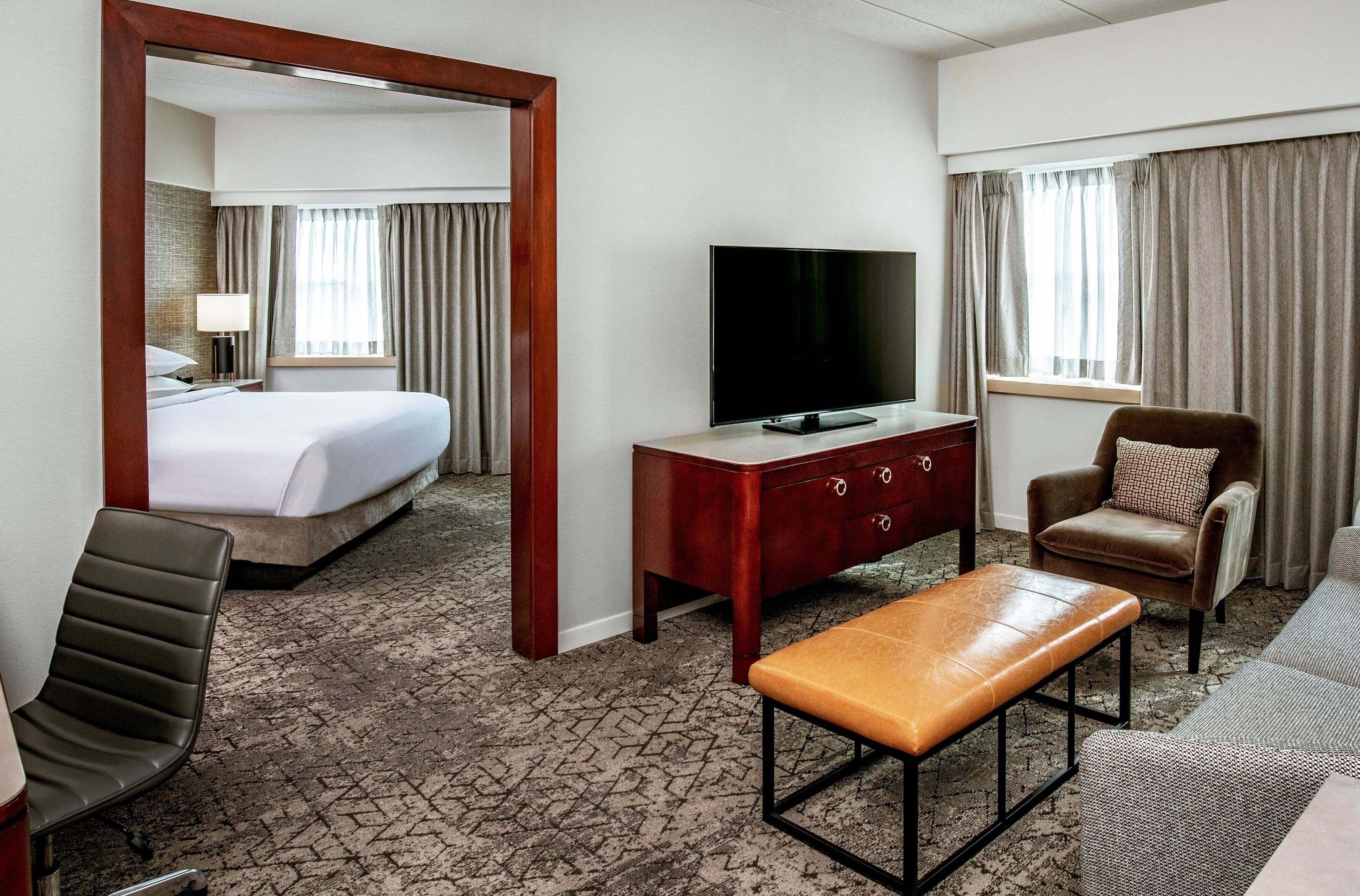 Quarto de hotel com cama, televisão, escrivaninha, cadeira e sofá.