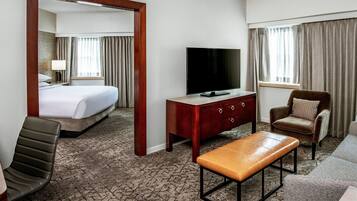 Quarto de hotel com cama, televisão, escrivaninha, cadeira e sofá.
