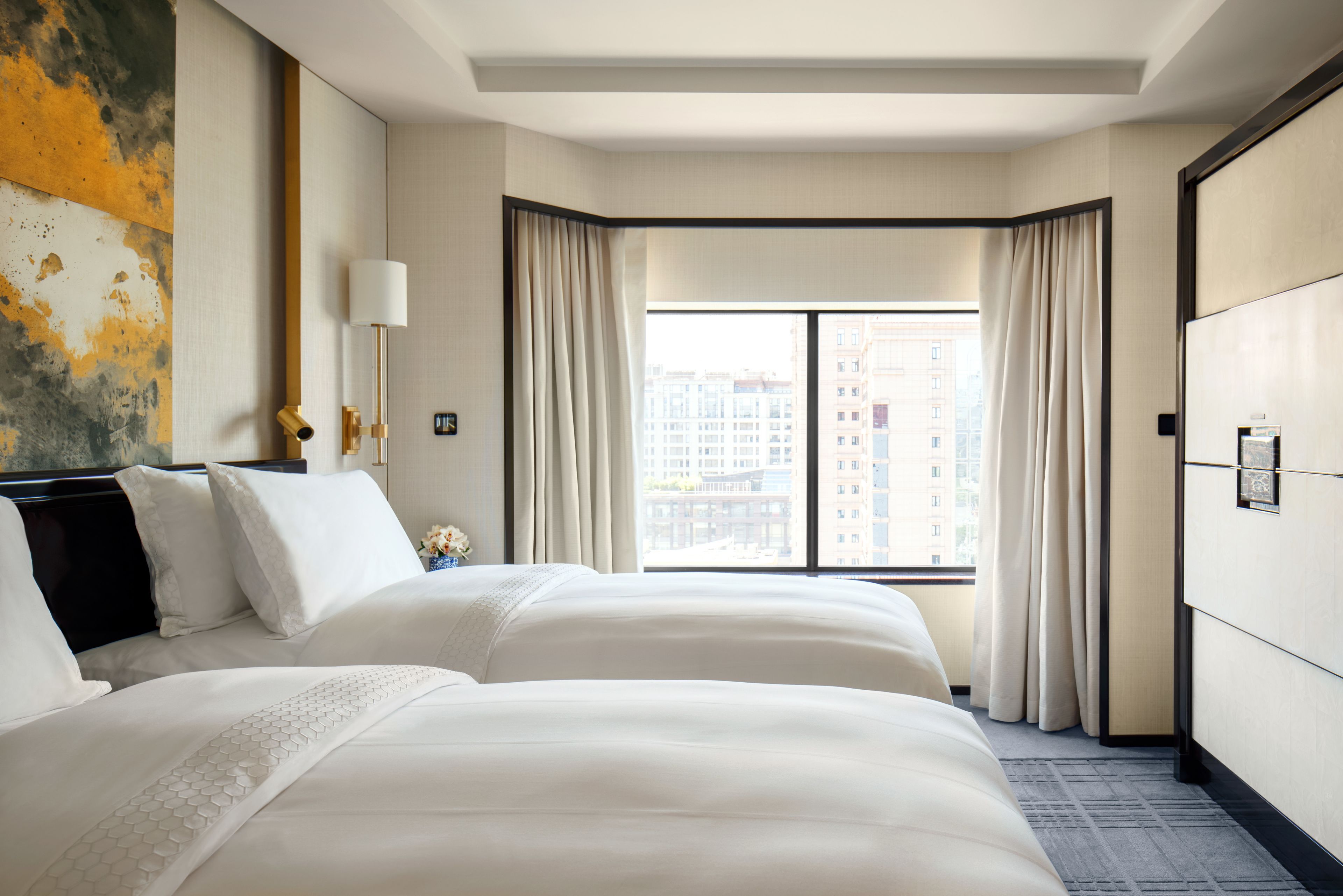 Quarto de hotel com uma cama grande, janela com cortinas e vista para edifícios.