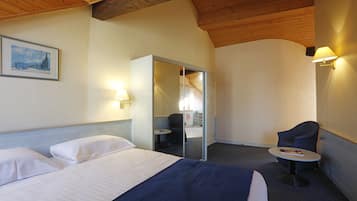 Quarto de hotel com cama, uma cadeira, uma mesinha e um espelho.