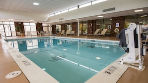 Piscina interior com faixas demarcadas, cadeira de salva-vidas e espreguiçadeiras à beira da piscina.