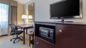 Quarto de hotel com televisão, micro-ondas, escrivaninha, cadeira e uma janela grande com cortinas.