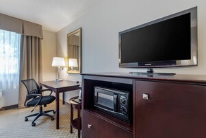 Quarto de hotel com televisão, micro-ondas, escrivaninha, cadeira e uma janela grande com cortinas.