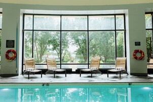 Área da piscina com quatro espreguiçadeiras e grandes janelas que oferecem vista para árvores.