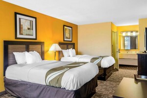 Quarto de hotel com duas camas, banheiro com espelho e pia, e obras de arte nas paredes.