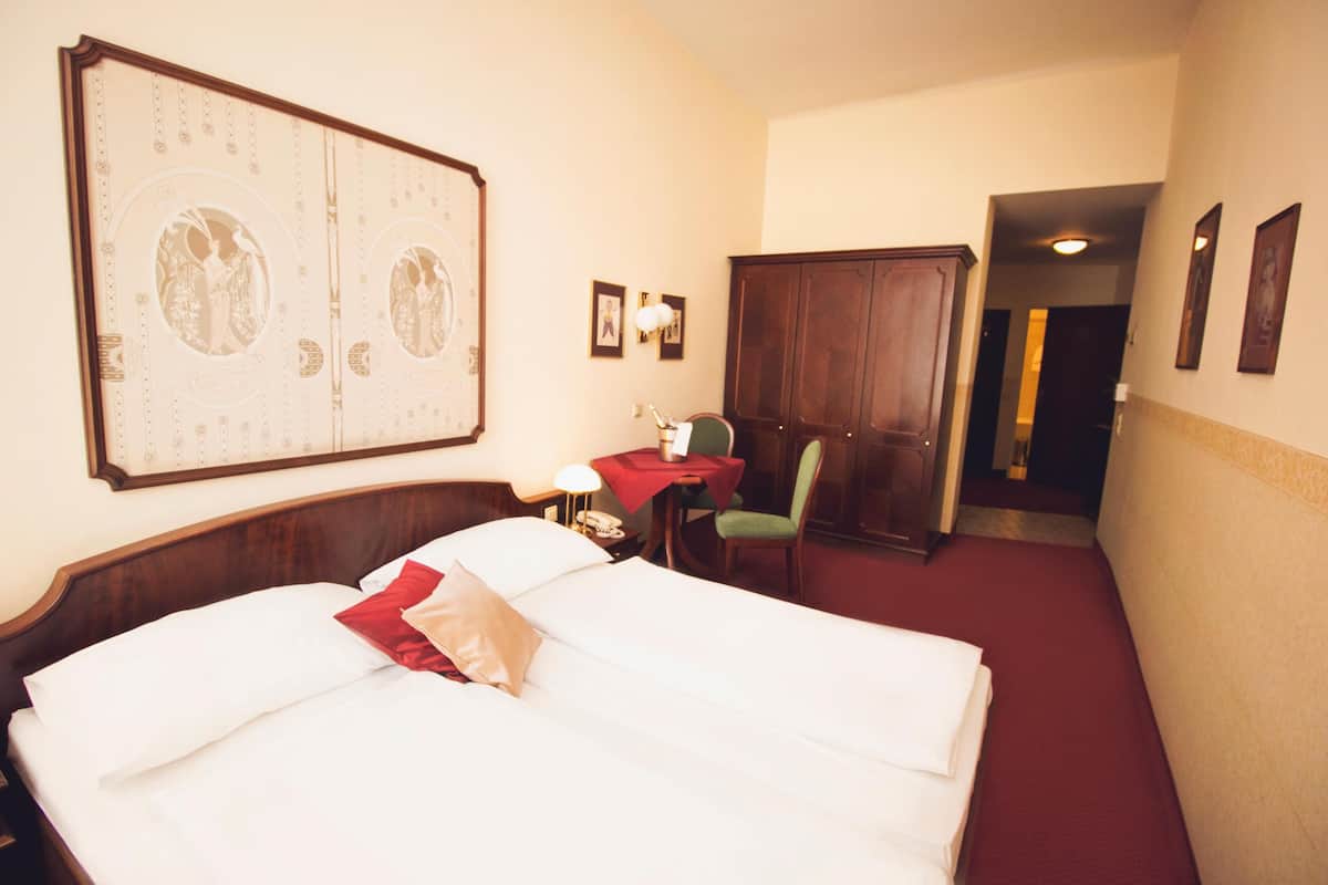 Quarto de hotel com uma cama grande, uma escrivaninha, uma cadeira, um guarda-roupa e uma obra de arte pendurada na parede.
