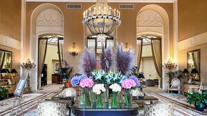 Um hall imponente com um grande candelabro, arranjos florais e móveis clássicos.