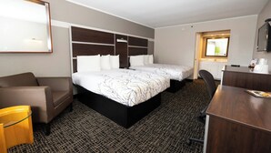 Quarto de hotel com duas camas, uma escrivaninha, uma cadeira, um sofá e uma pequena lixeira.